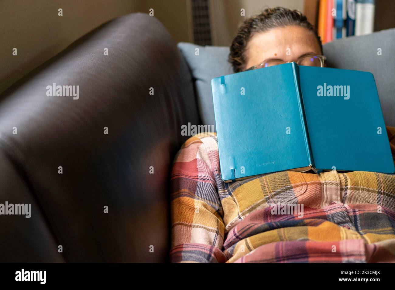 A person on sofa at home napping while reading a book Stock Photo - Alamy