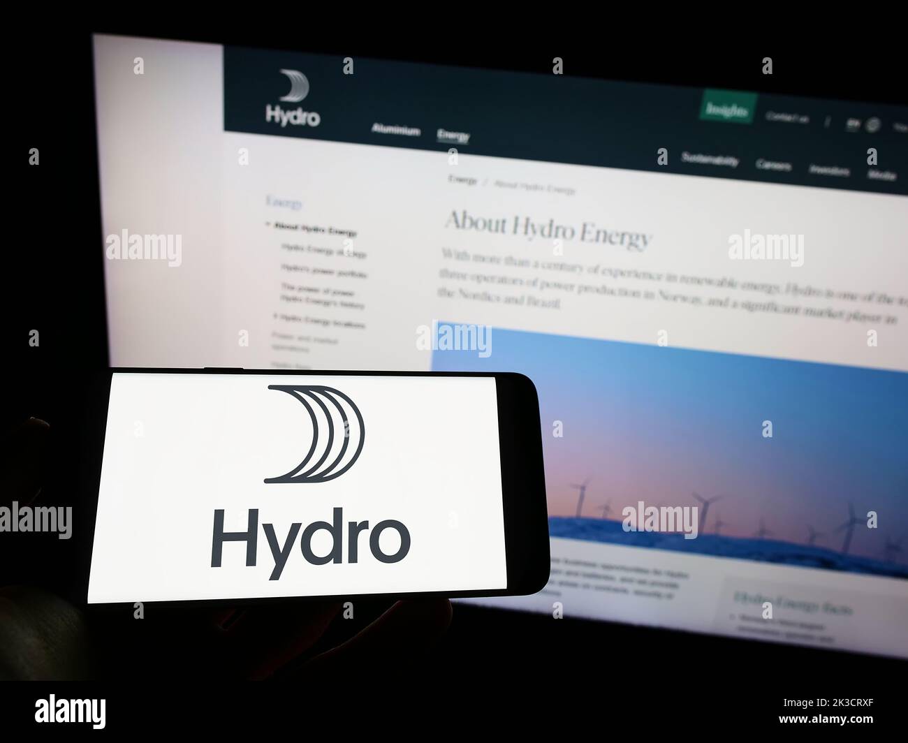 Person holding mobile phone with logo of Norwegian aluminium company Norsk Hydro ASA on screen ...