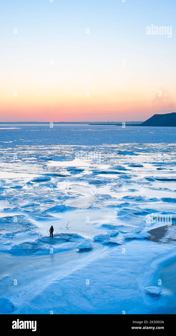Aerial view - lonely man walk on ice on sunset over a frozen sea ...