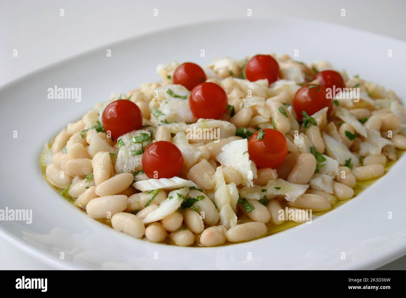 A closeup of a white dish with beans and tomatoes Stock Photo - Alamy