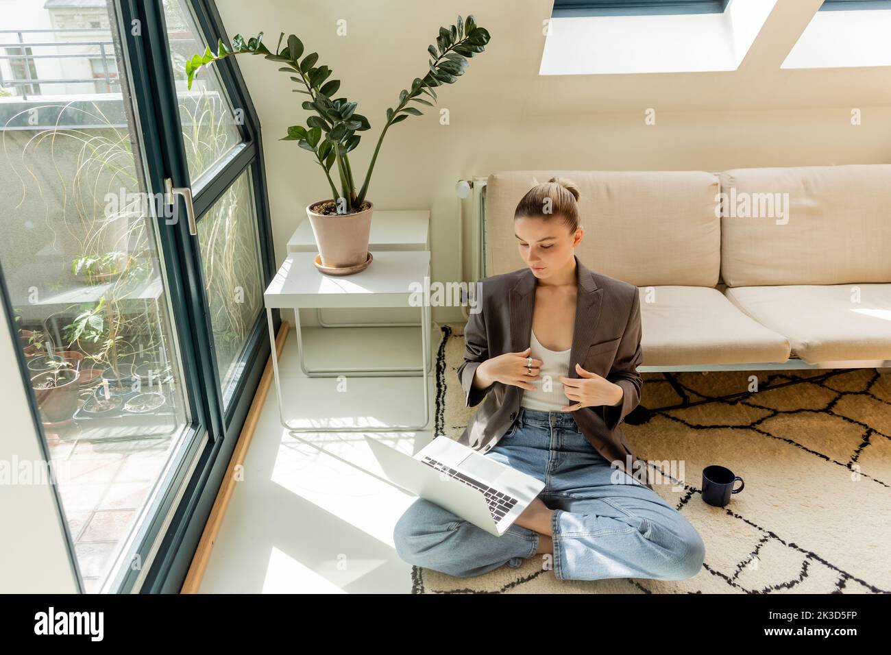 Freelancer in jacket looking at laptop near cup on couch in living room ...