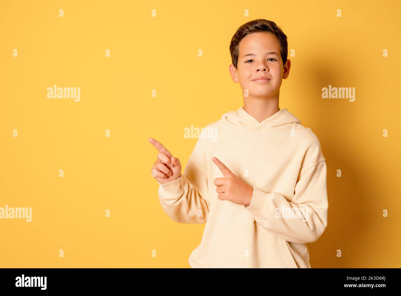 Portrait of cheerful boy pointing to the side - isolated over yellow ...