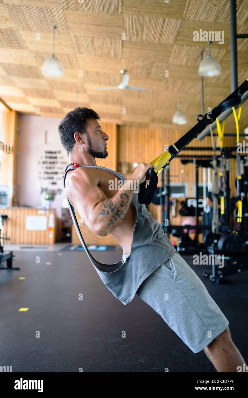 Vertical photo of a strong man doing exercises with trx in a gym Stock ...