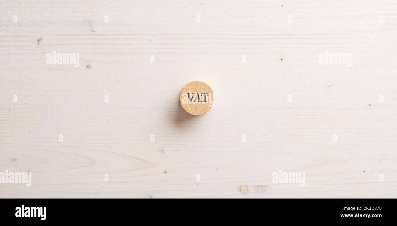 Wooden cut circle with a VAT sign on it placed over simple blank wooden ...