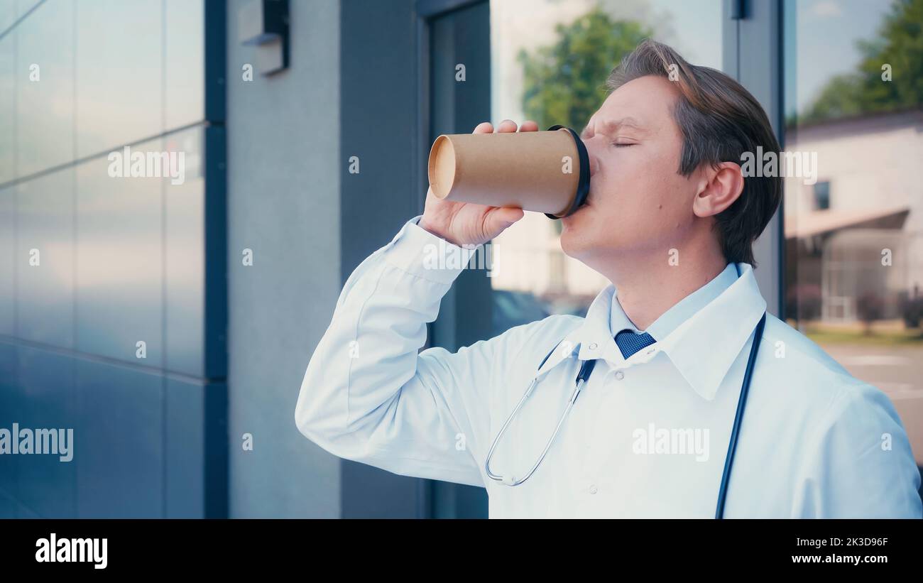 doctor with stethoscope drinking coffee near building of clinic,stock ...