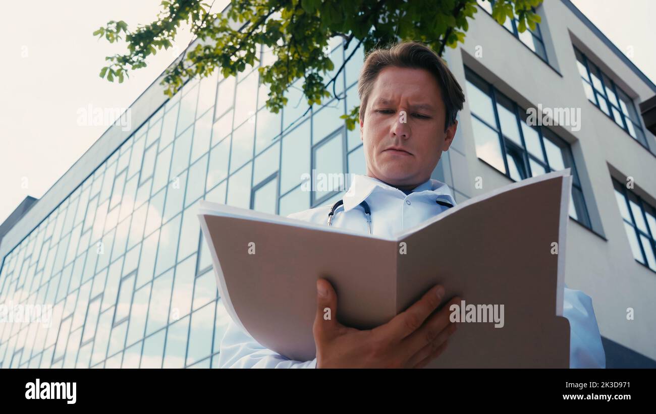 low angle view of doctor looking in folder with documents near hospital ...