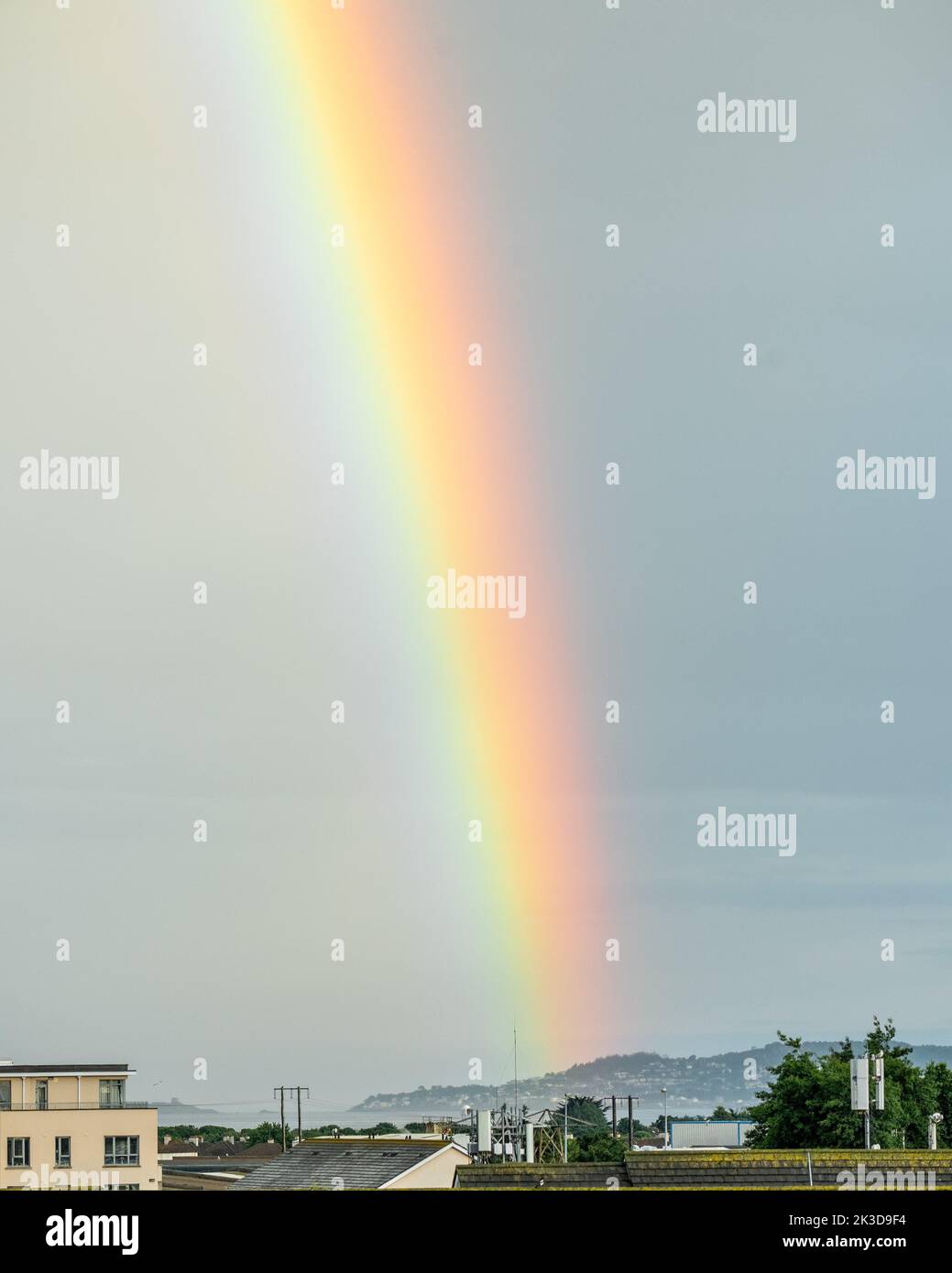 The vertical view of the rainbow raising from the hill to the gray sky ...