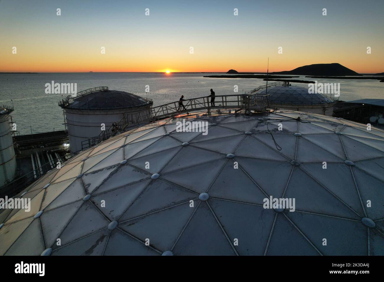 Two workers on top of a sphere dome building near a coast during sunset ...