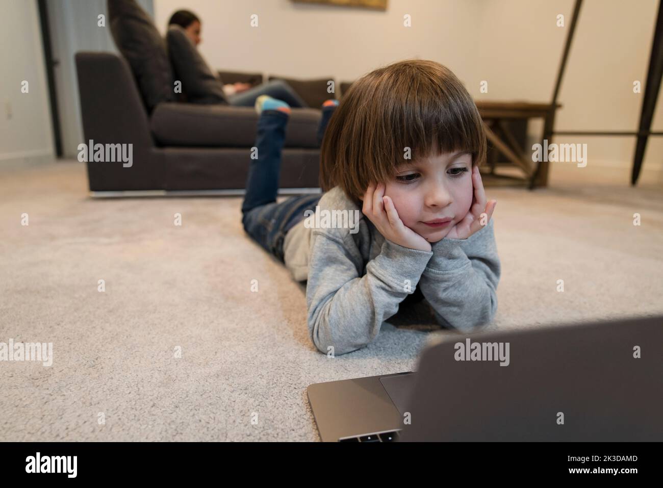 Cute brunette boy watching video at laptop on living room floor Stock ...