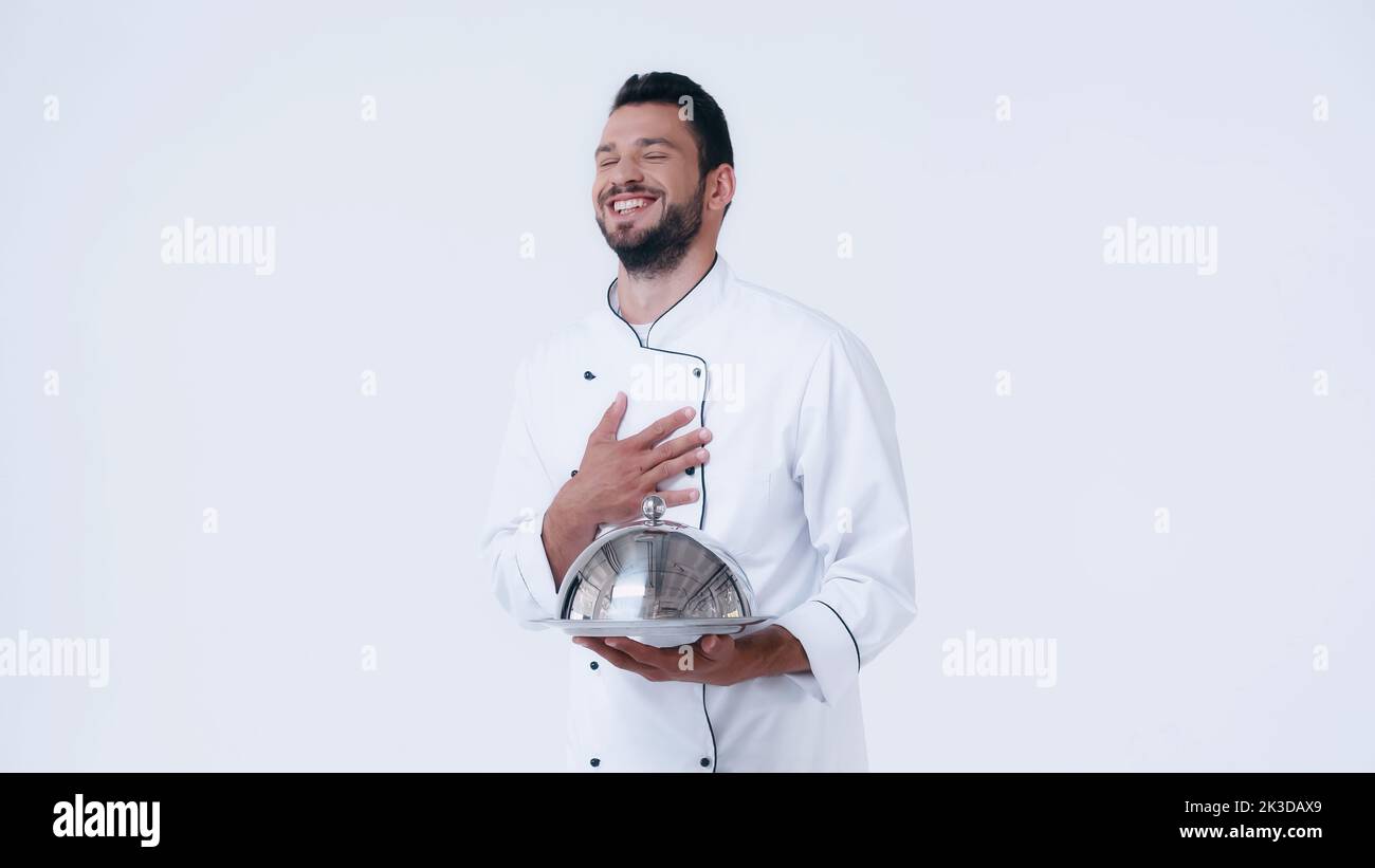 laughing chef with serving platter and cloche touching chest isolated ...
