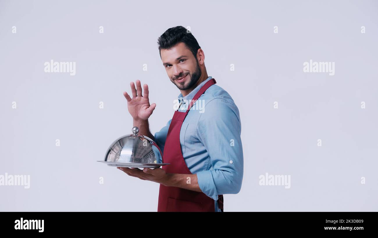 positive waiter waving hand while holding serving dish with cloche ...