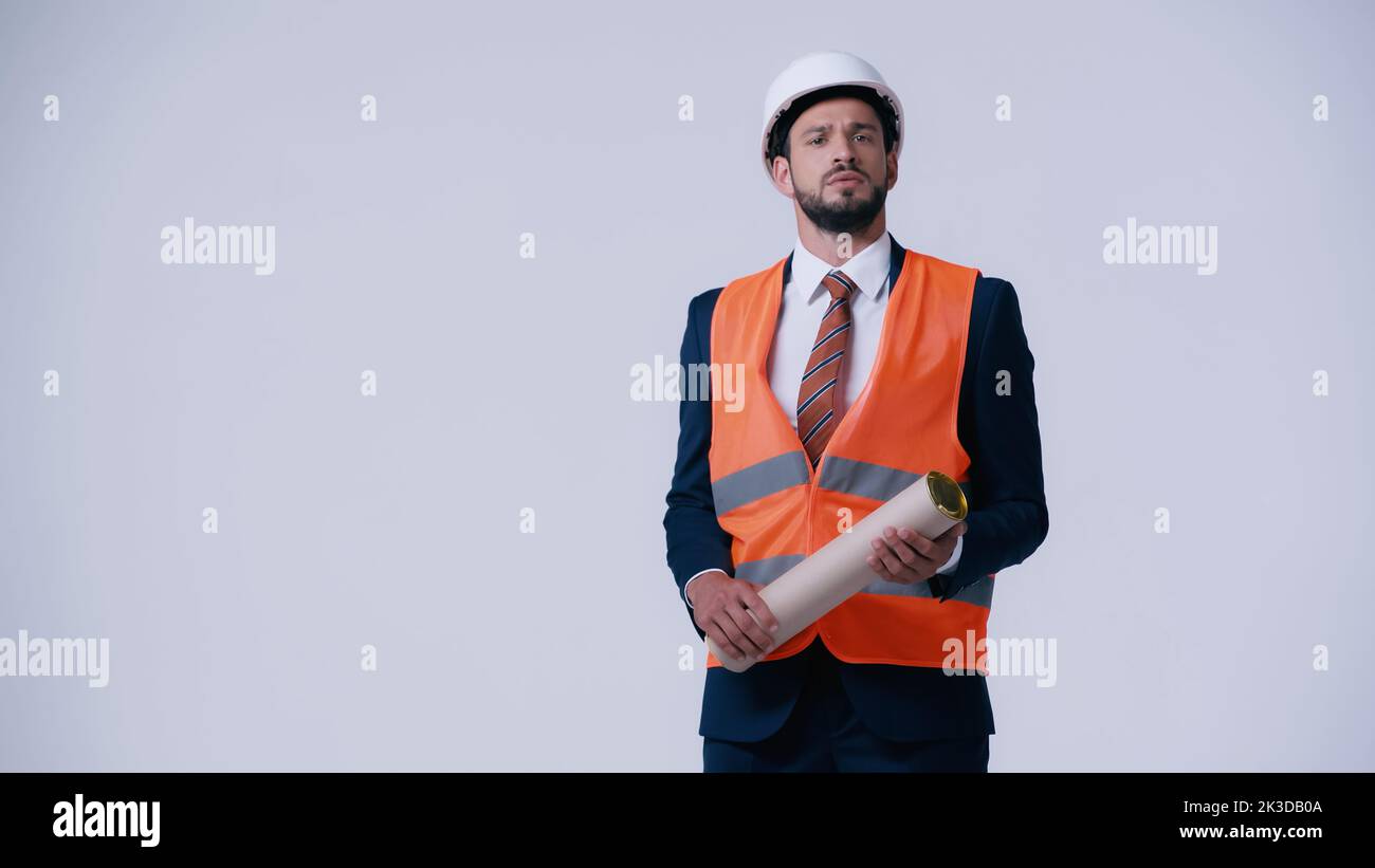 serious architect in formal wear and safety vest holding blueprint tube ...