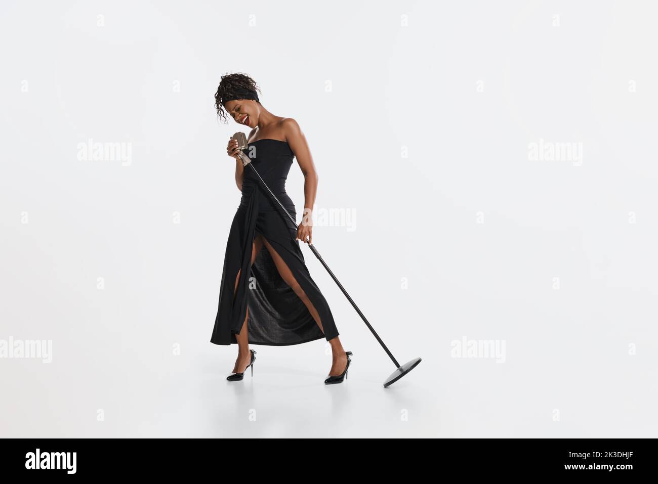 Studio shot of female african singer with microphone isolated on white ...
