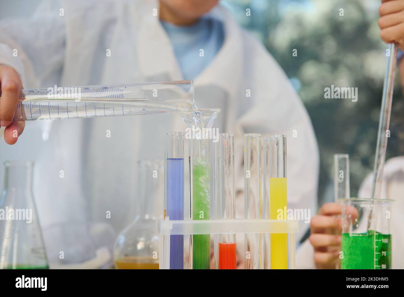 Focus on pouring water from a measuring cylinder into test tubes with ...