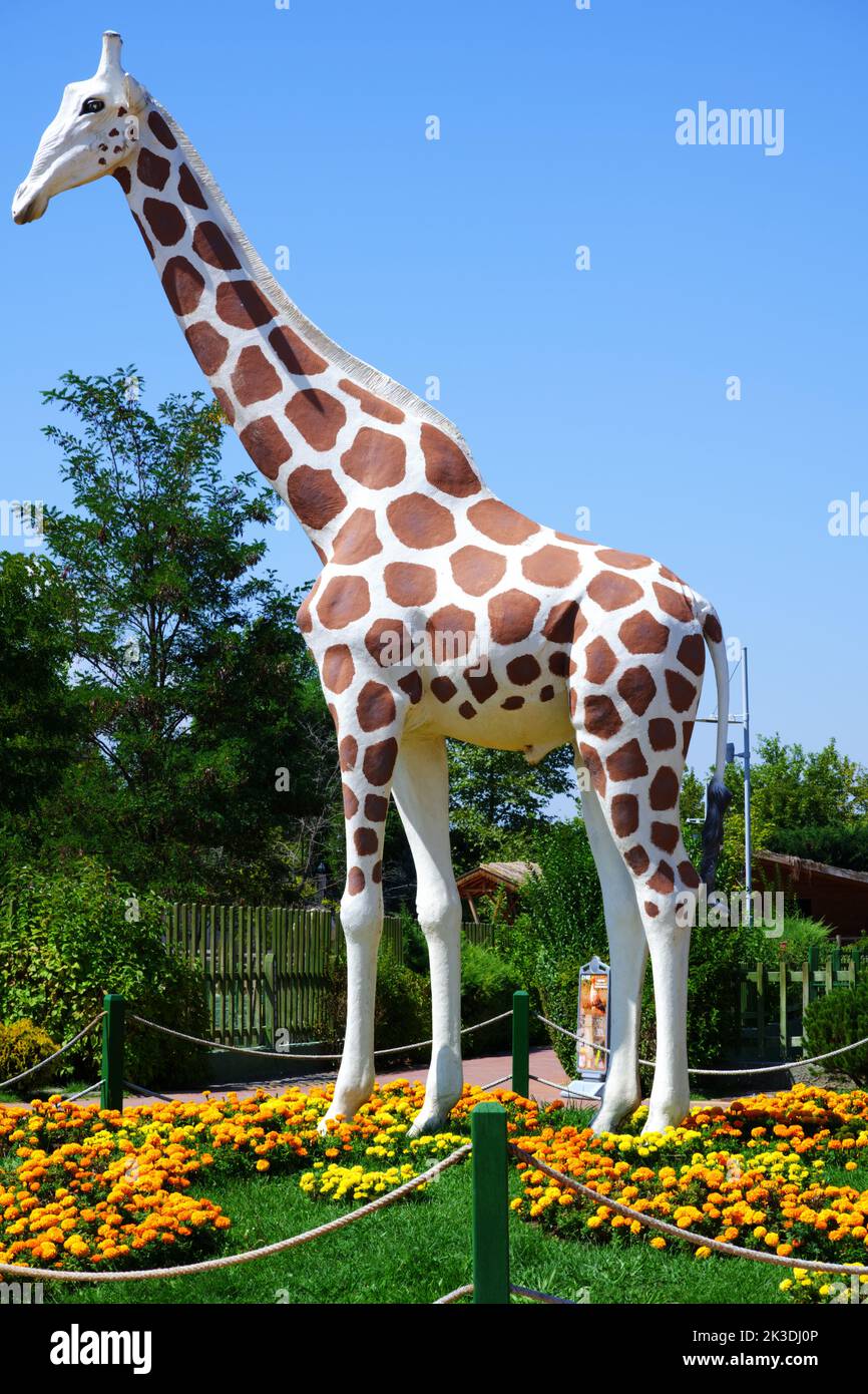 Plastic giraffe statue at park with colorful flowers in a sunny day ...