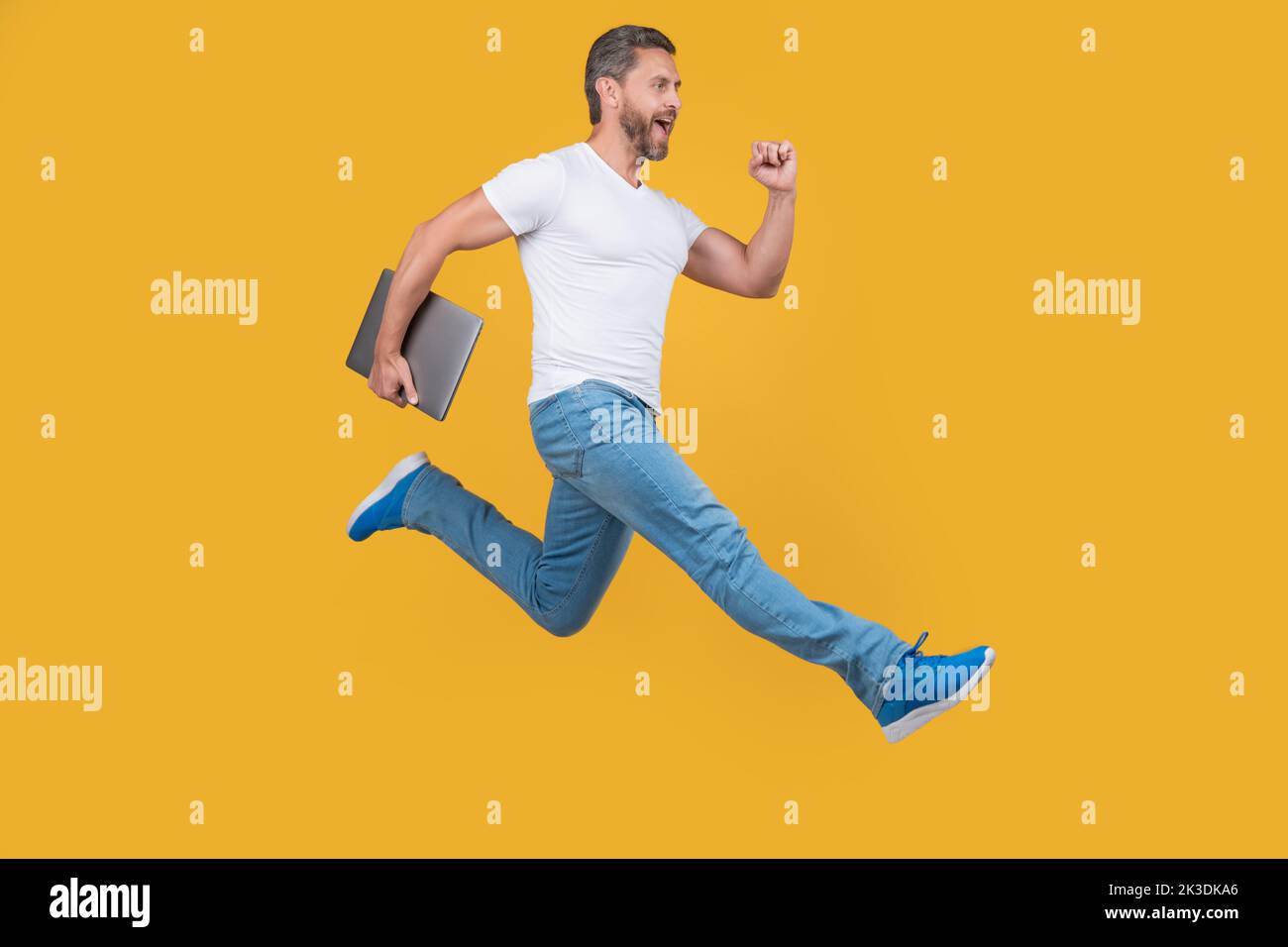 man running with computer. man hold laptop isolated on yellow studio ...