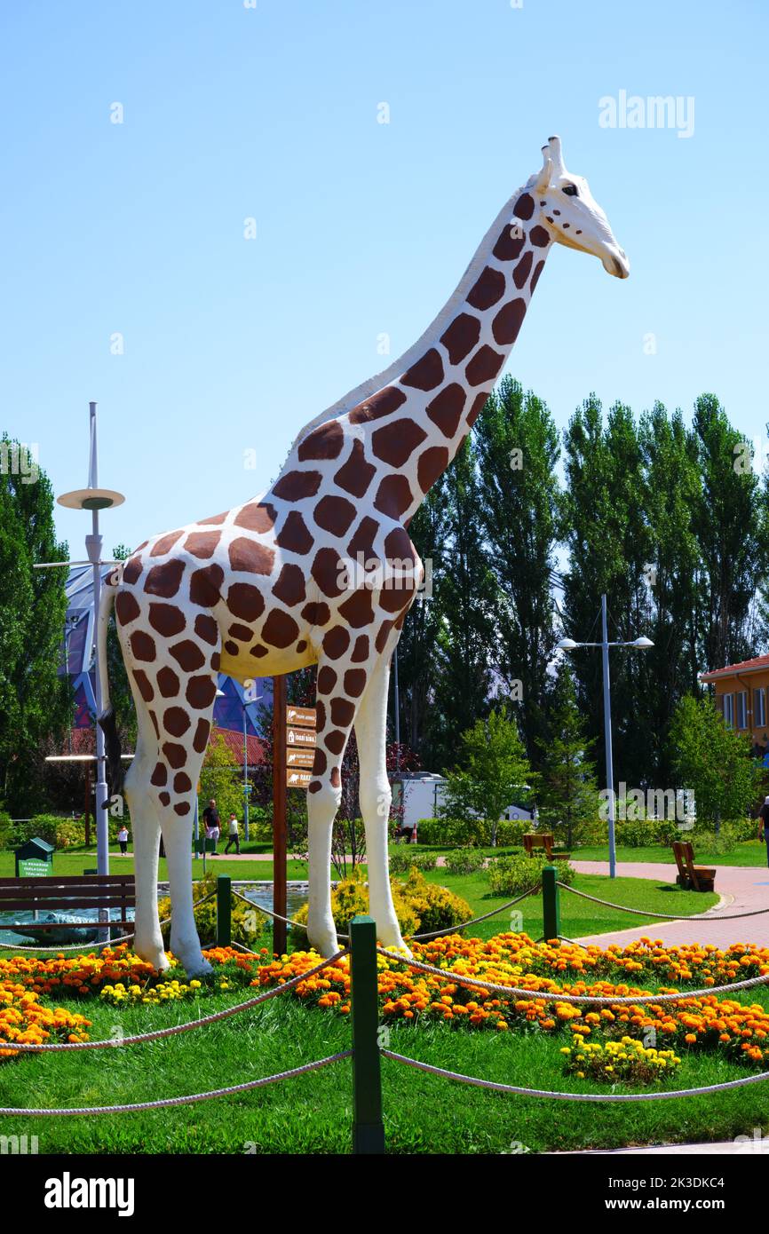 Plastic giraffe statue at park with colorful flowers in a sunny day ...