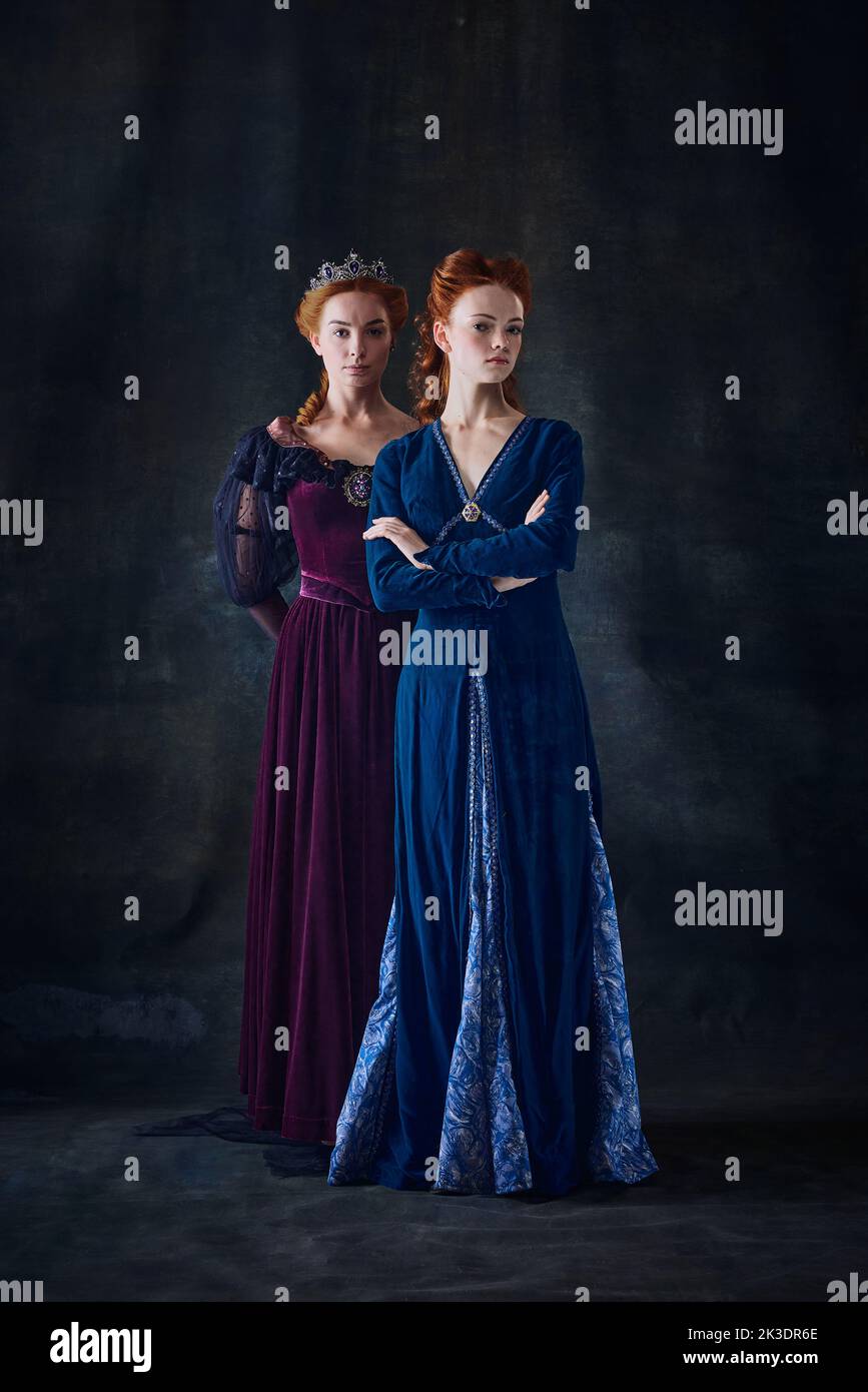 Portrait of two beautiful women in image of queens isolated over dark ...