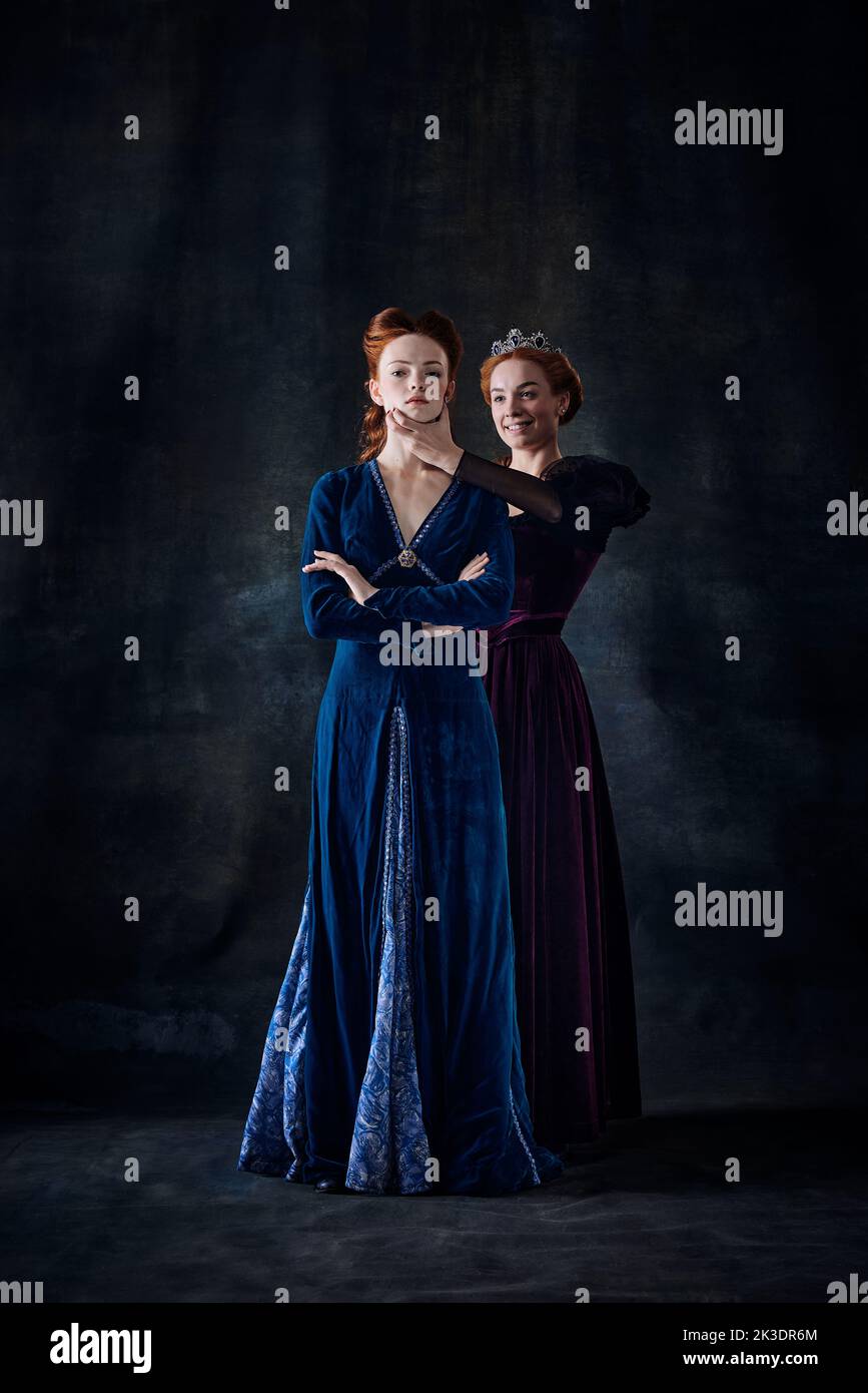 Portrait of two beautiful women in image of queens isolated over dark ...