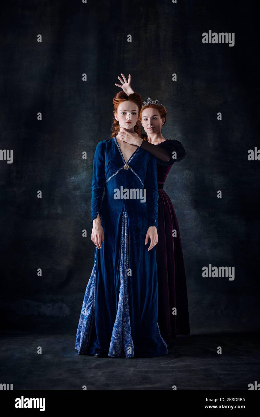 Portrait of two beautiful women in image of queens isolated over dark ...