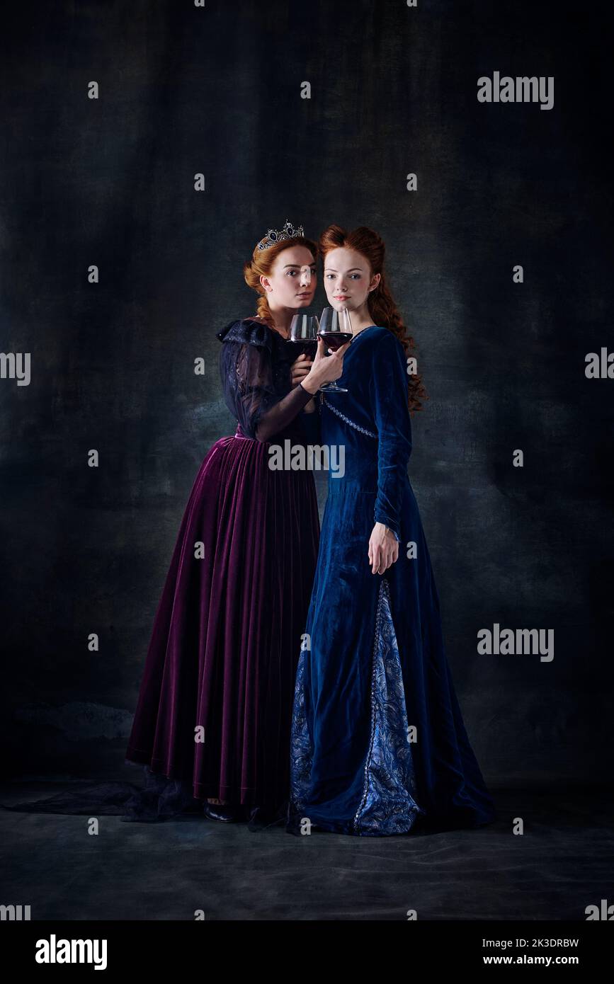 Portrait of two beautiful women in image of queens with wine glasses ...