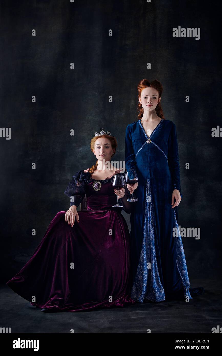 Portrait of two beautiful women in image of queens isolated over dark ...