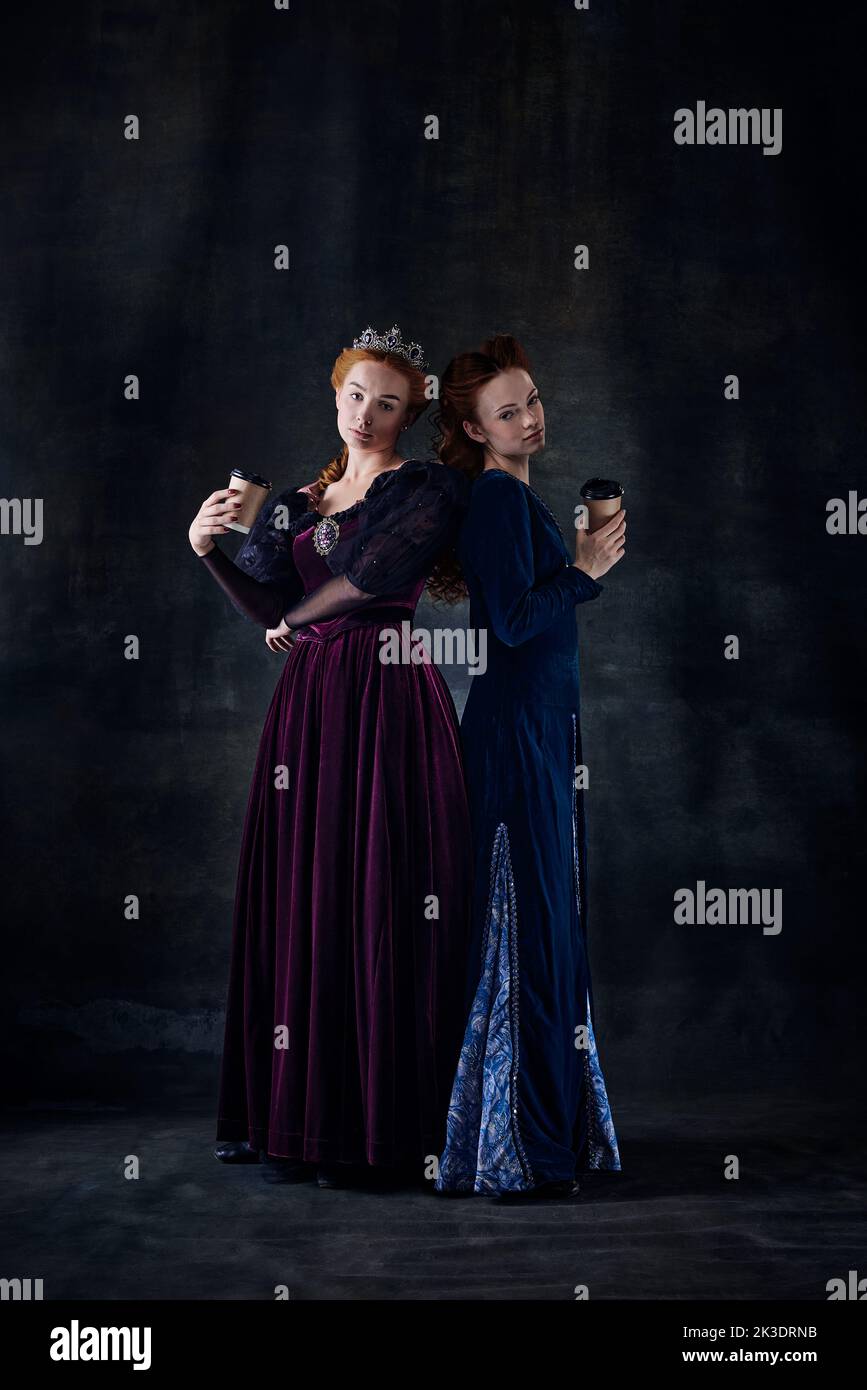 Portrait of two beautiful women in image of queens isolated over dark ...