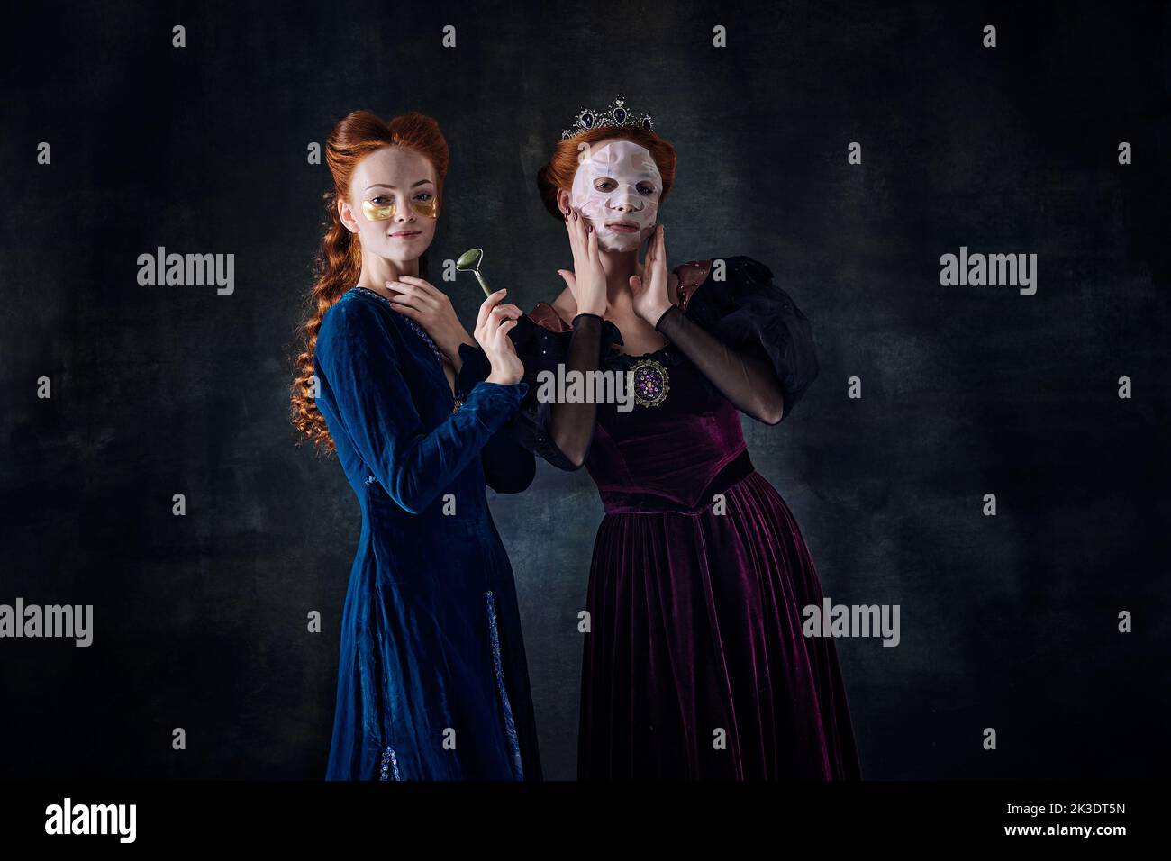 Portrait of two beautiful women in image of queen and princess applying ...