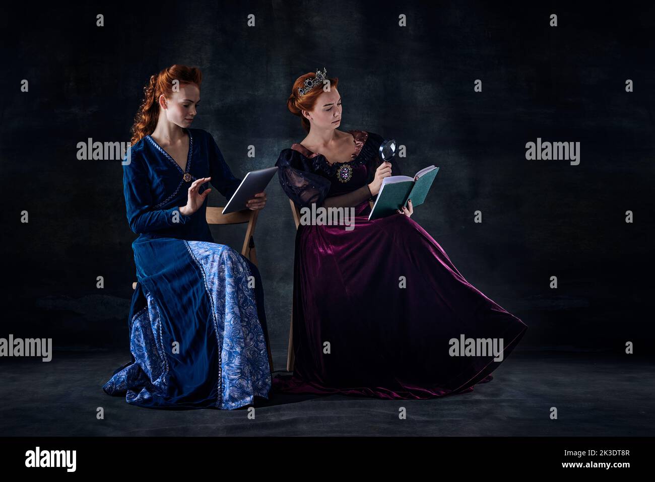 Portrait of two beautiful women in image of queens reading notes and ...