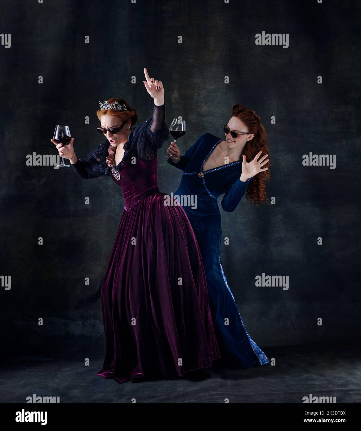 Portrait of two beautiful women in image of queens dancing with wine in ...