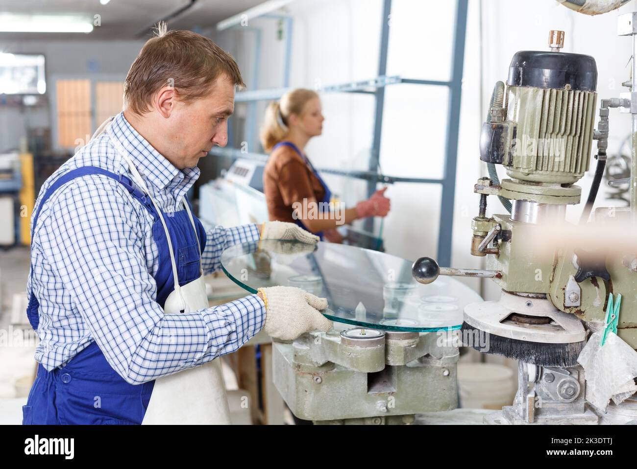 Male glazier with female assistant working on curved glass beveling ...