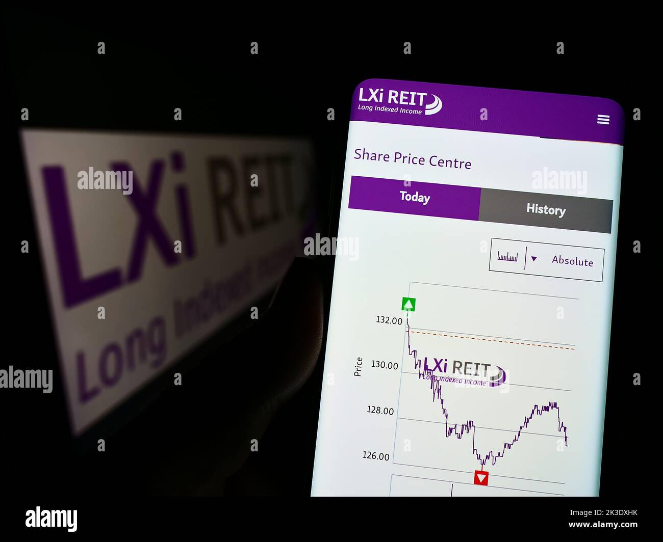 Person holding cellphone with webpage of British real estate company LXi REIT on screen in front ...