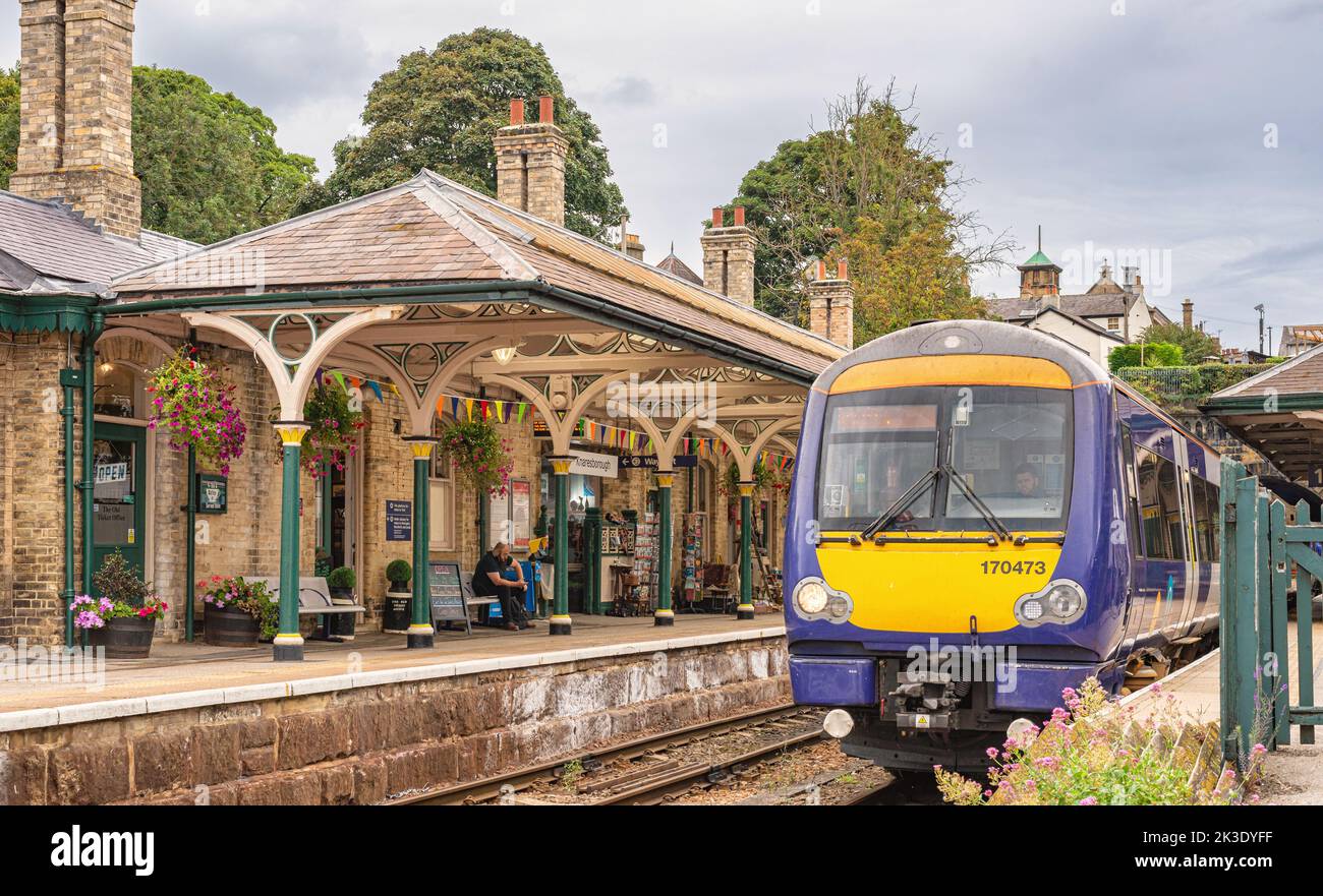 A train stops a small railway station. Colourful flower baskets hang ...