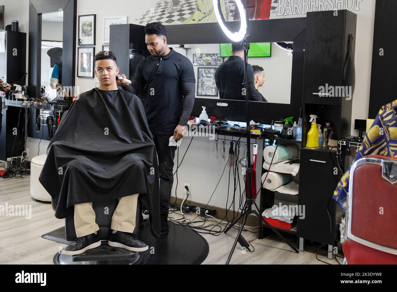 Barber with electric razor giving man haircut in barber shop Stock ...