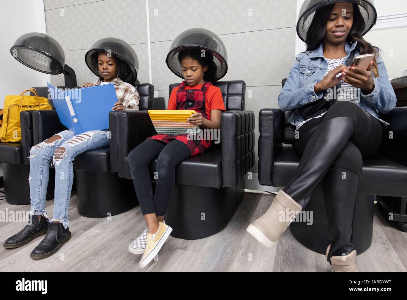 Mother and daughters under hairdryers, reading in hair salon Stock ...