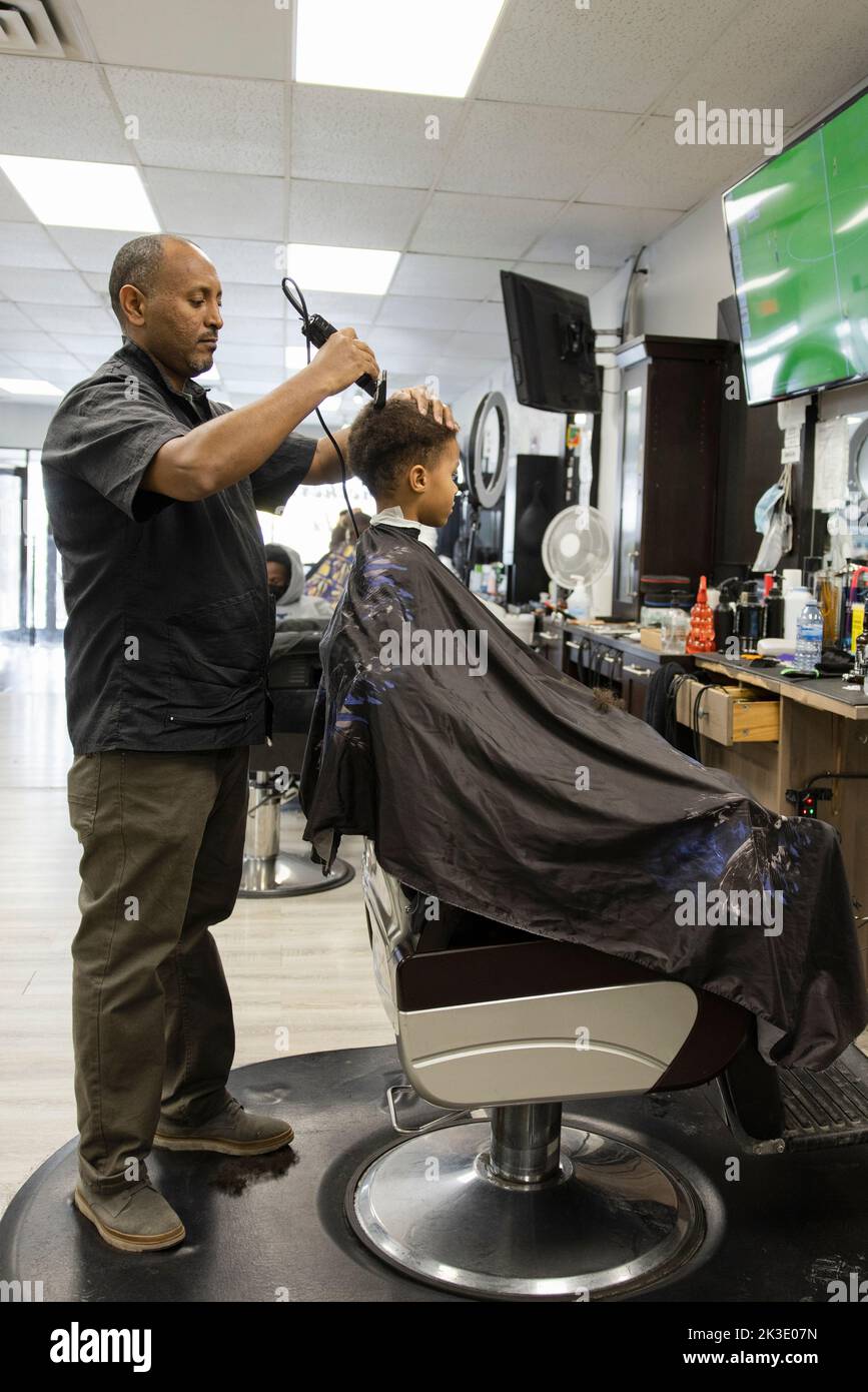 Barber with electric razor giving boy a haircut in barber shop Stock ...