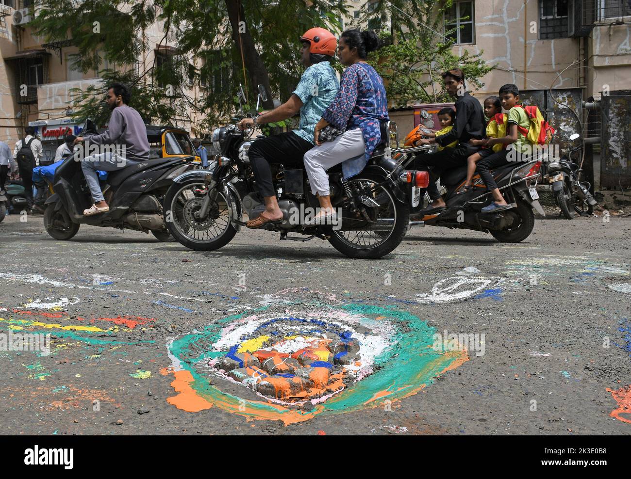Motorcyclists ride past a pothole painted in different colors in Mumbai ...