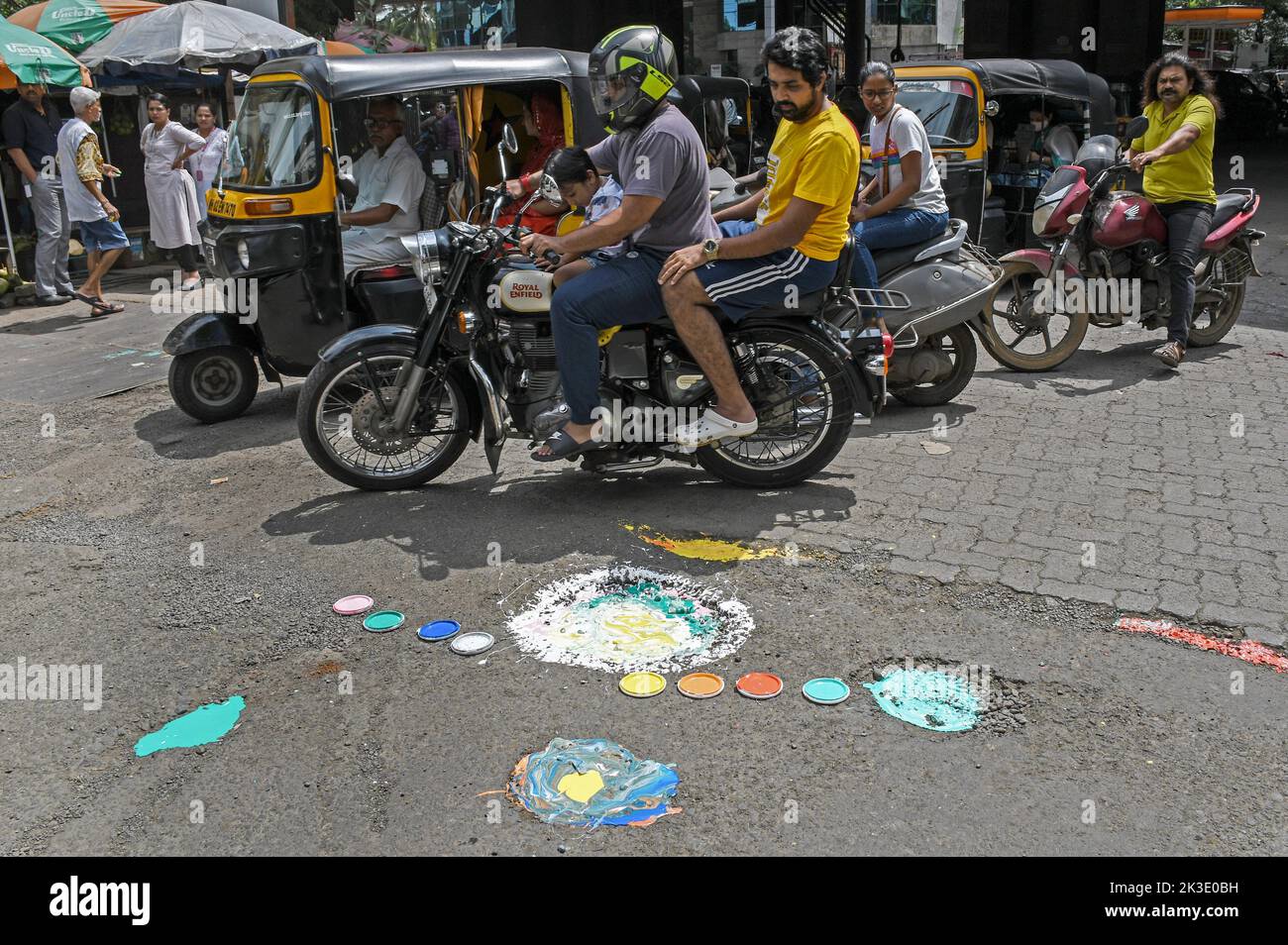 Motorcyclists ride past a pothole painted in different colors in Mumbai ...