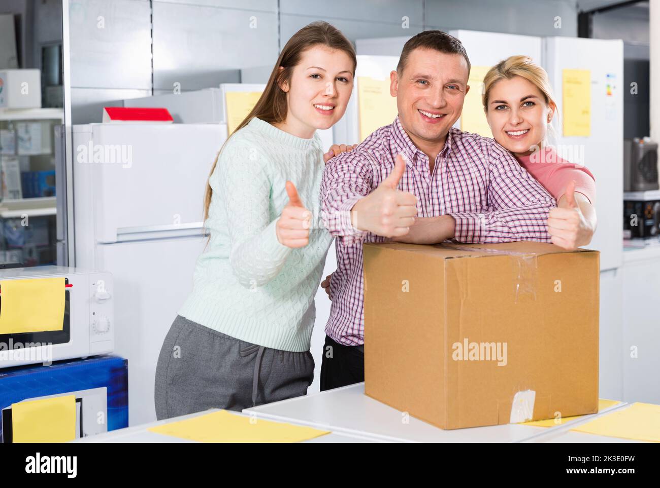 Positive family of three holding thumbs up in store with packed ...