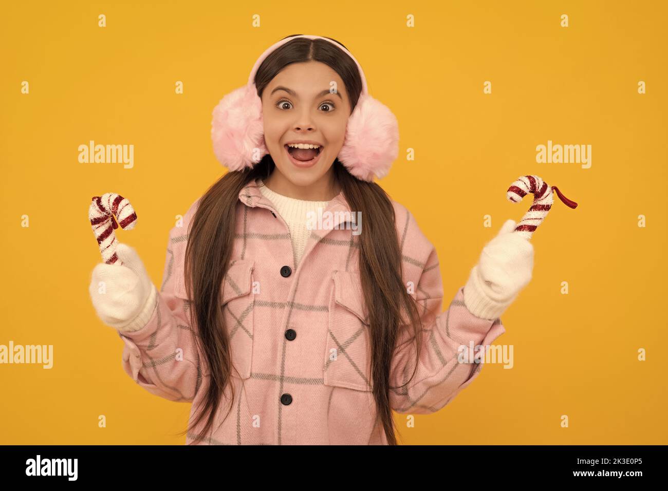 amazed kid in earmuffs and mittens hold candy stick on yellow ...