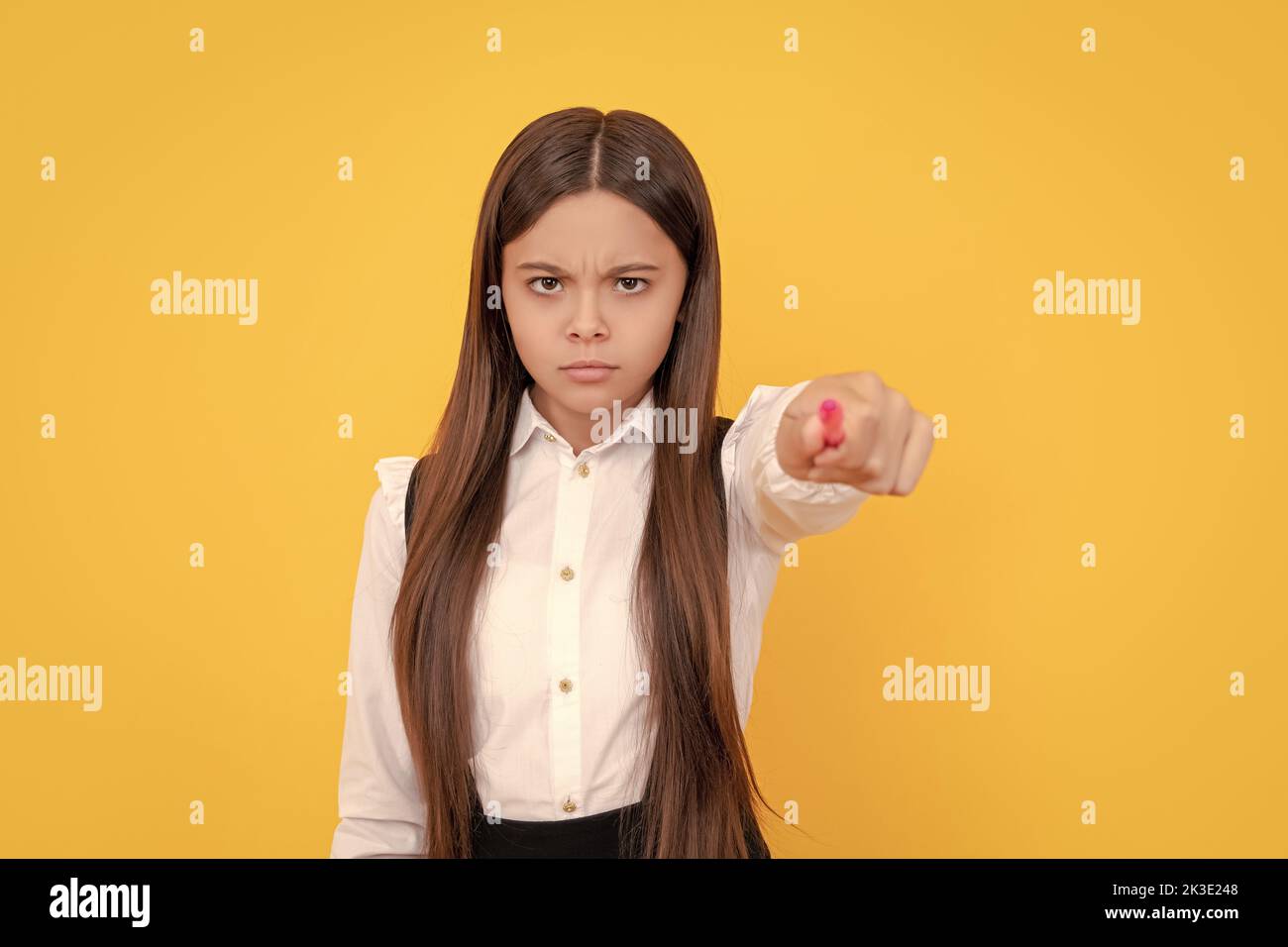 Serious frown school girl point pen putting out hand yellow background ...