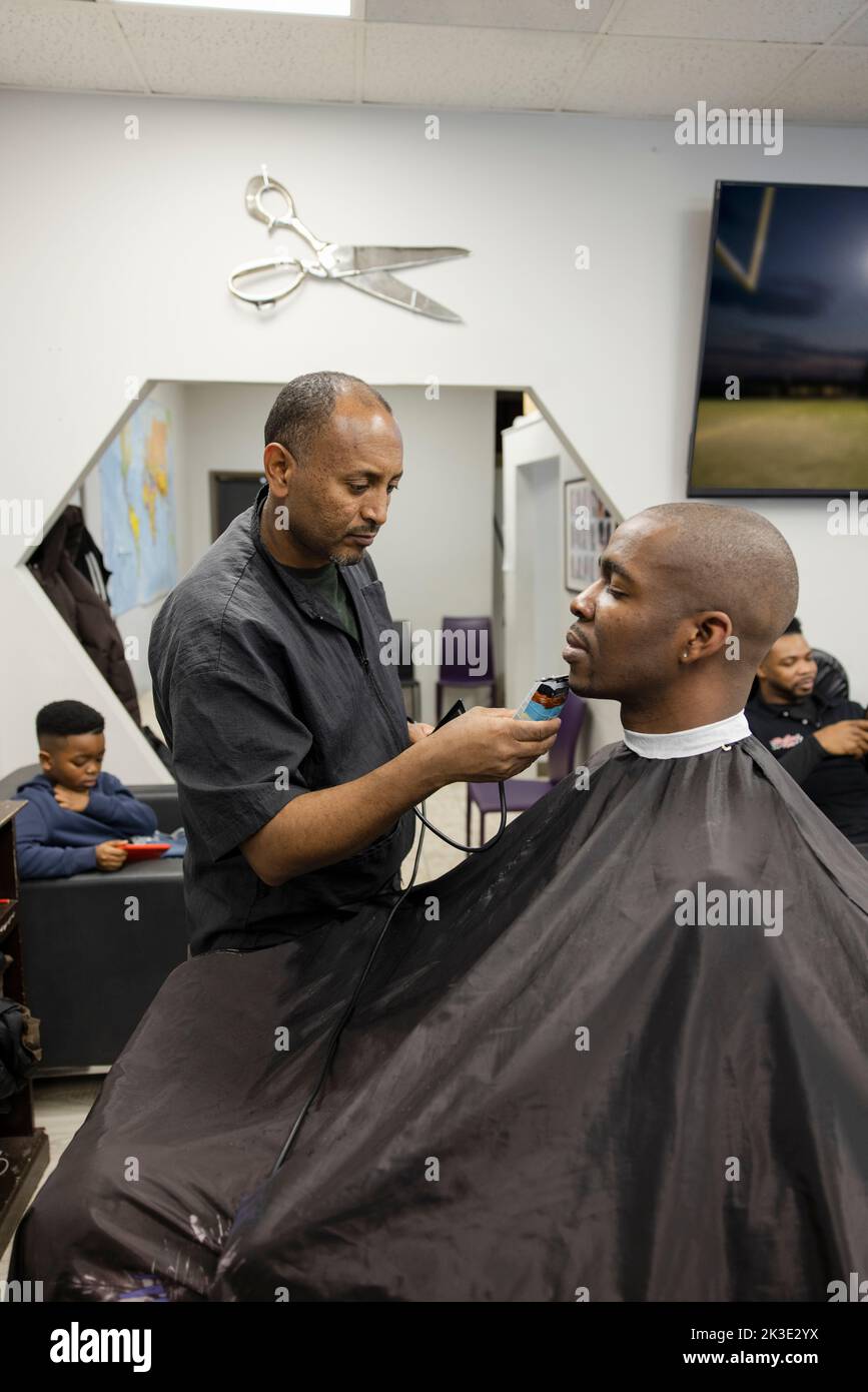 Barber with electric razor giving customer a shave in barber shop Stock ...
