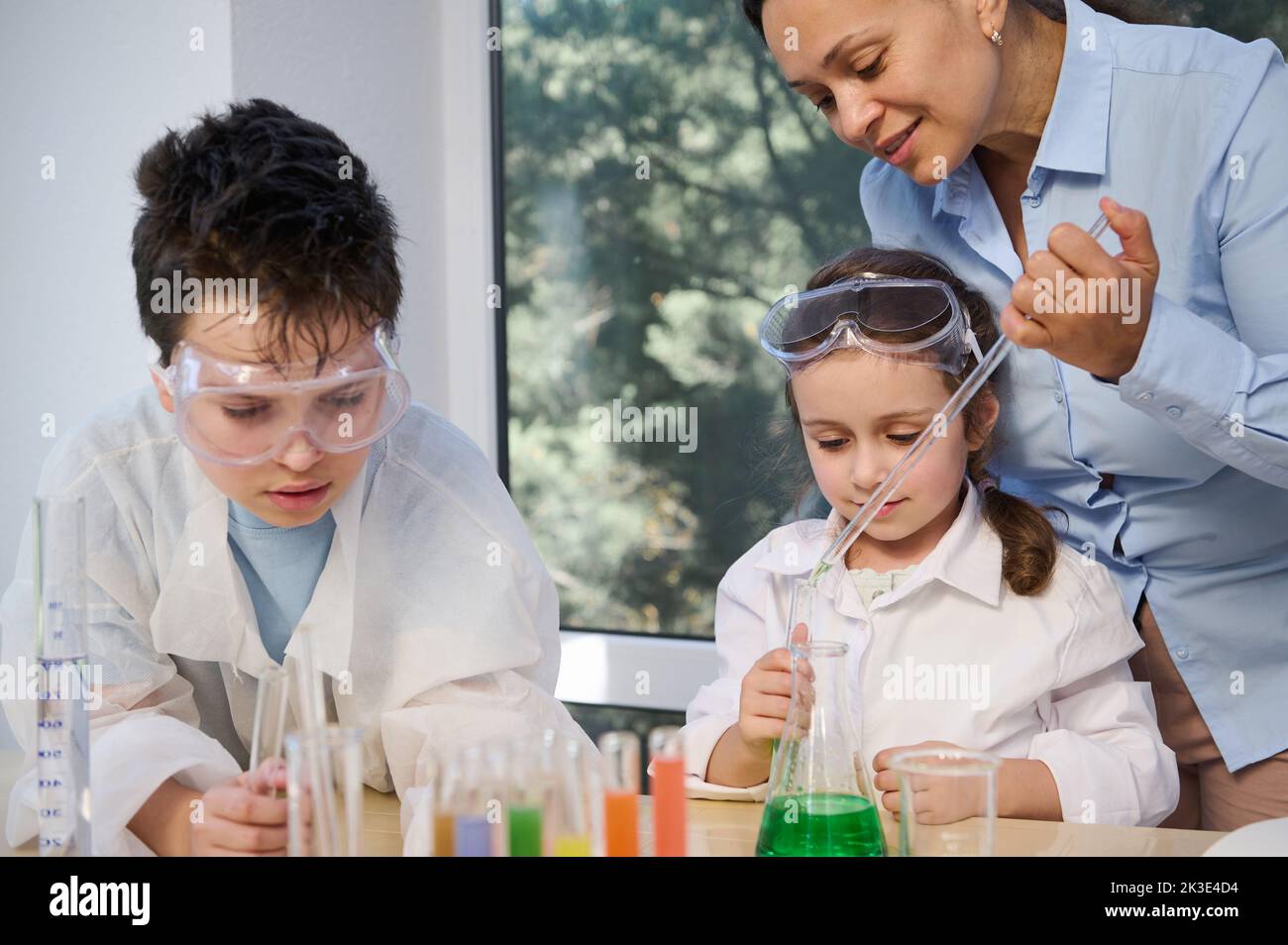 African American young woman teacher, explains chemistry class to smart kids, conducting ...