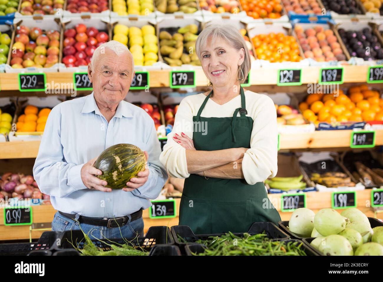Woman supermarket employee helping mature man to choose watermelon and ...