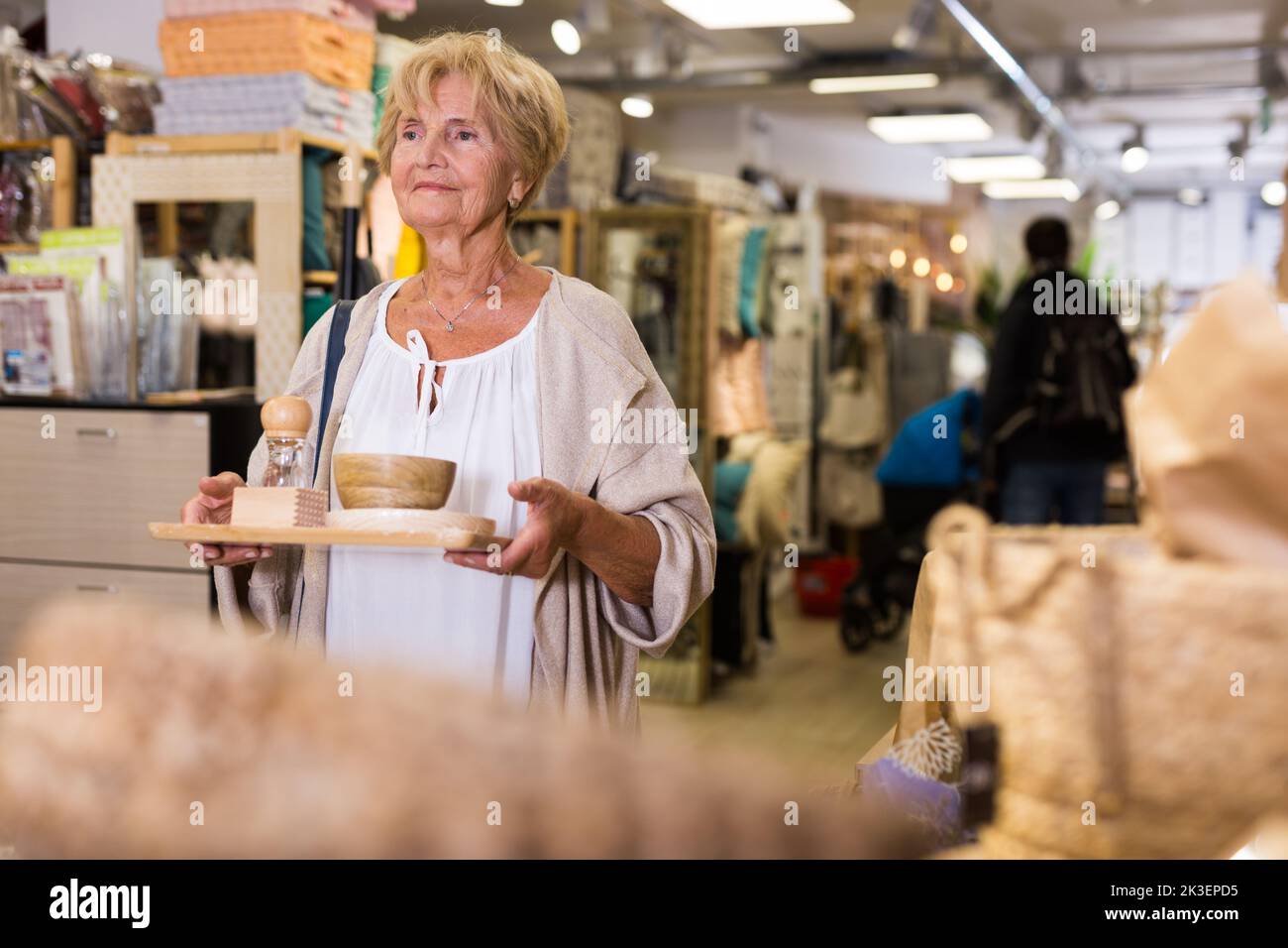 Senior woman customer holding purchases and walking in household goods ...