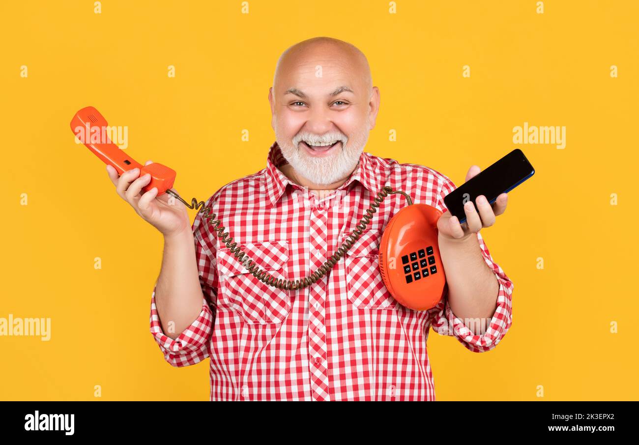 happy senior man with retro telephone and modern smartphone on yellow ...
