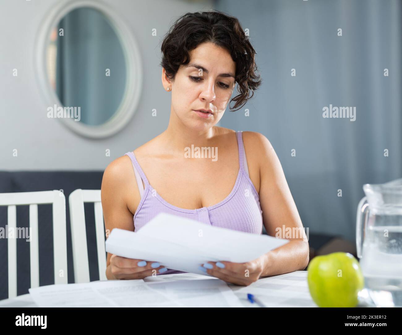 Sad woman reading letter while sitting at table at home Stock Photo - Alamy