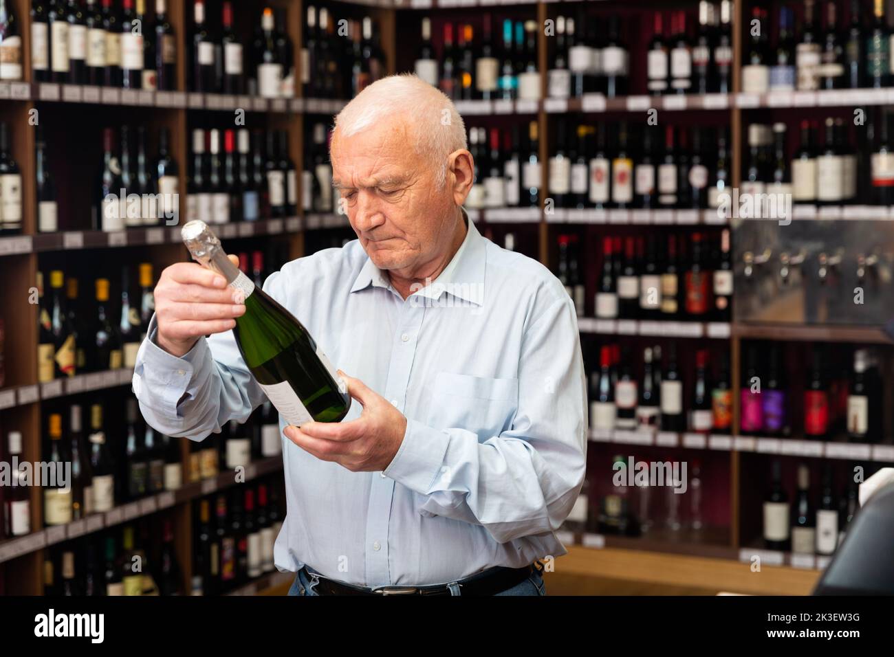 Attentive elderly man chooses champagne in a liquor store Stock Photo ...