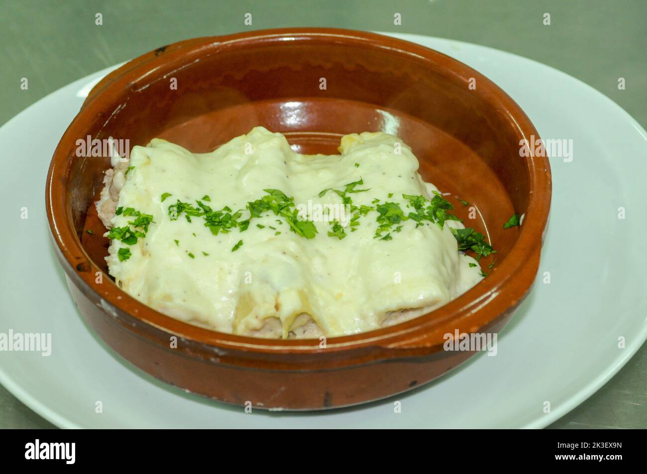 Portion of cannelloni with meat, cream sauce and cheese in a clay pot ...