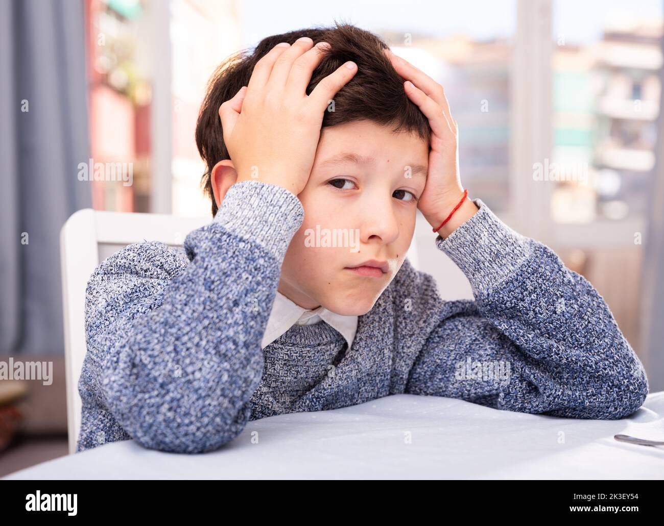 Unhappy boy sitting at table in the room Stock Photo - Alamy